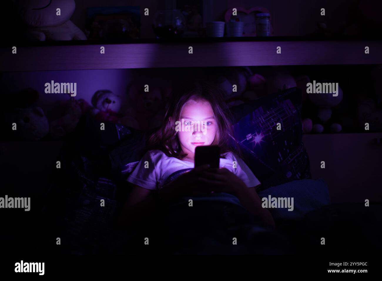 A 10-11-year-old girl browsing her smartphone under the blanket at ...