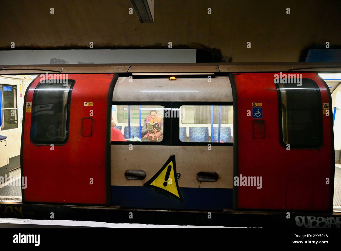 a woman reads a book on the northern line tube at archway with ...