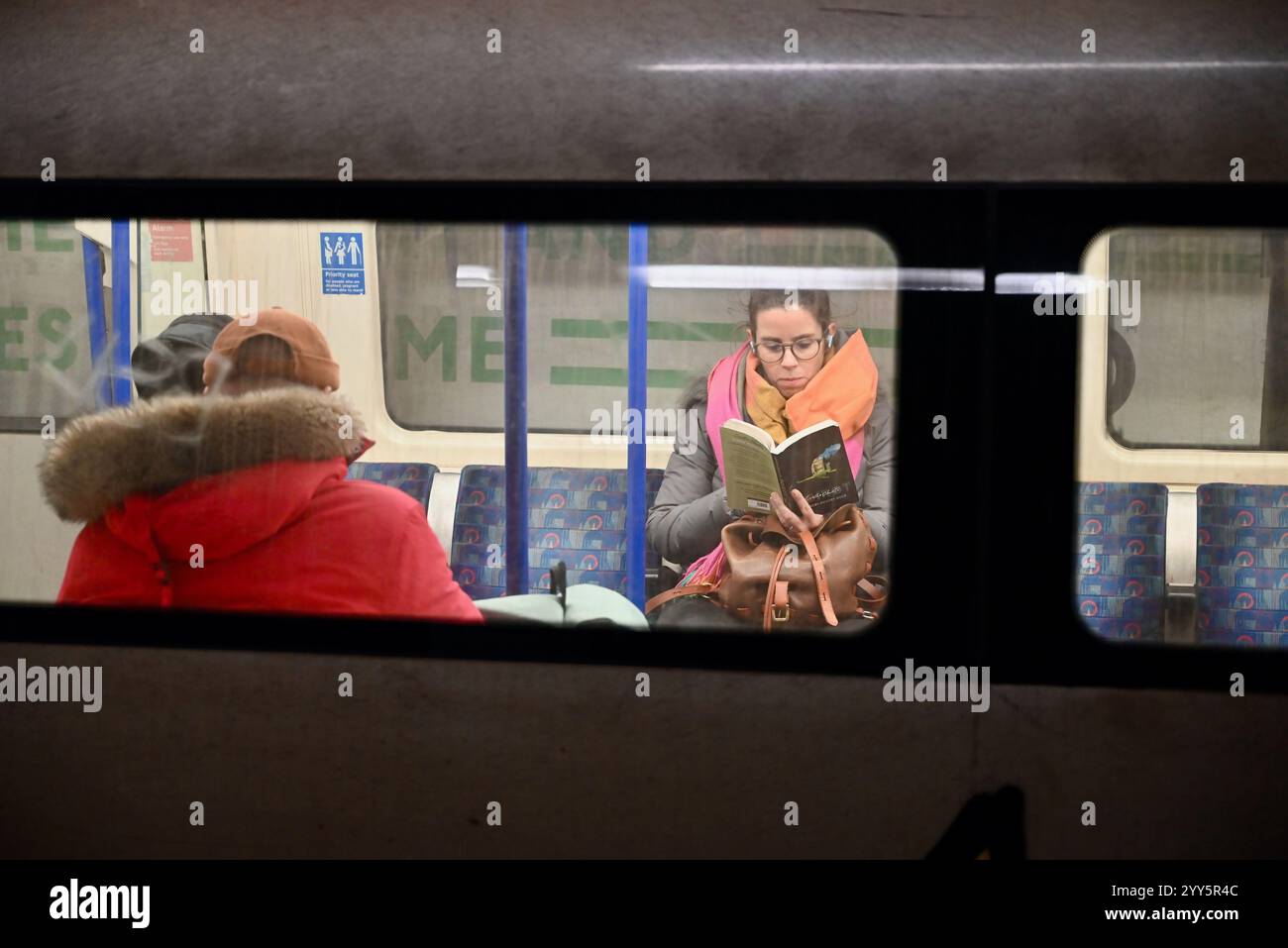 a woman reads a book on the northern line tube at archway with ...
