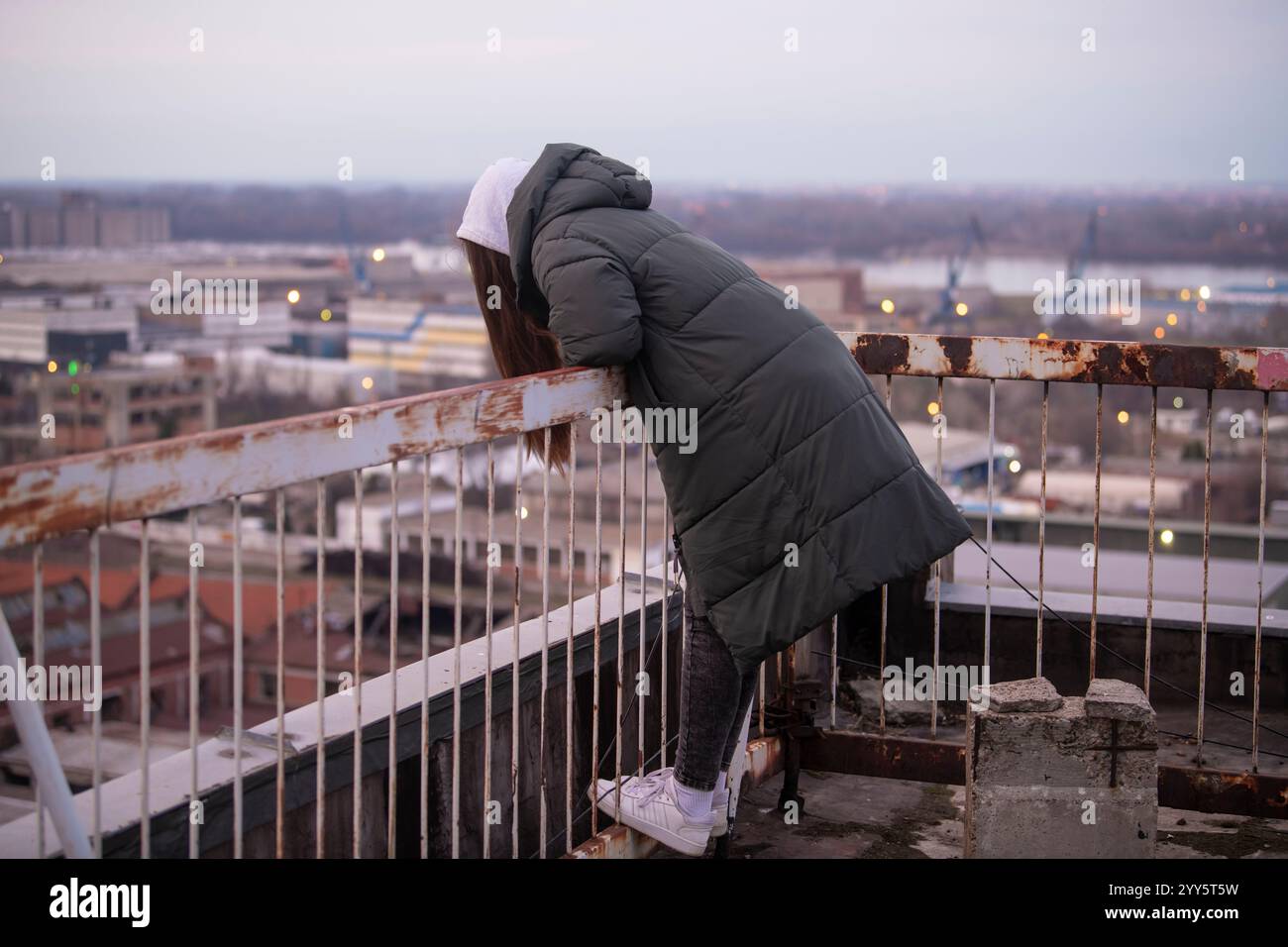 Depressed sad young female in jacket with hoodie standing on the edge ...