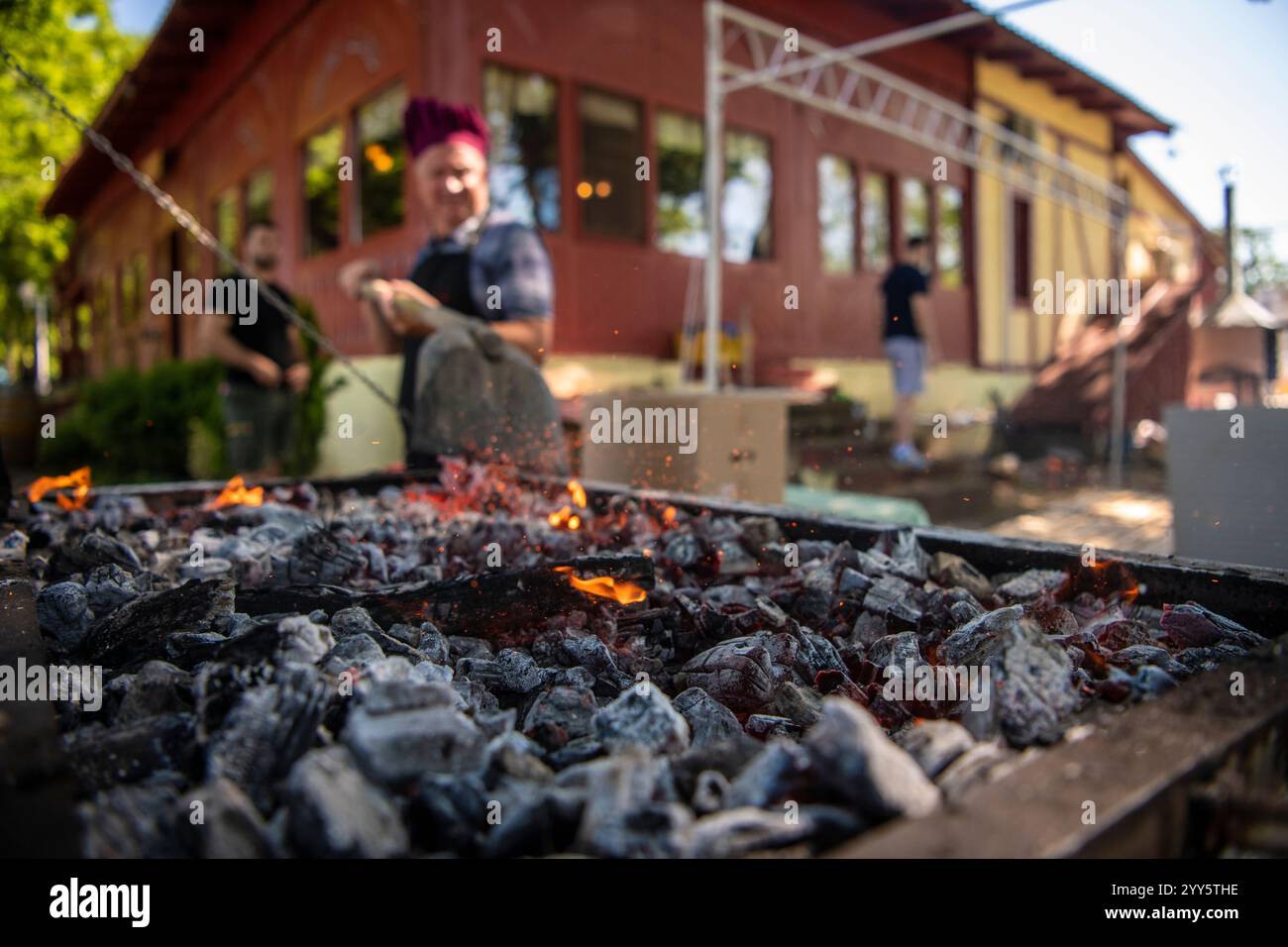 Chef with cook hat prepares barbecue grill pit with shovel. Glowing and ...