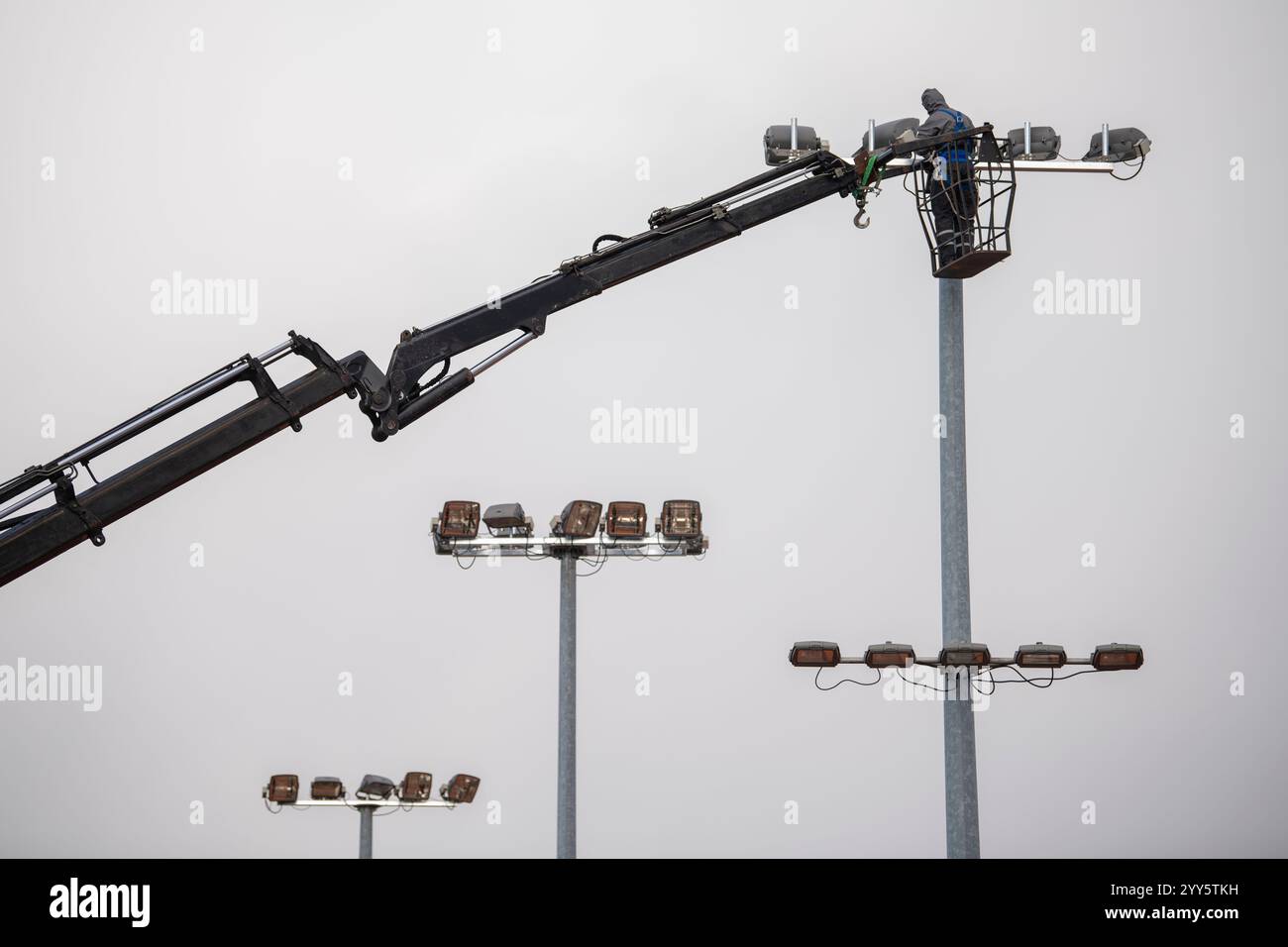 Electrician worker standing in hydraulic crane basket, fixing stadium ...