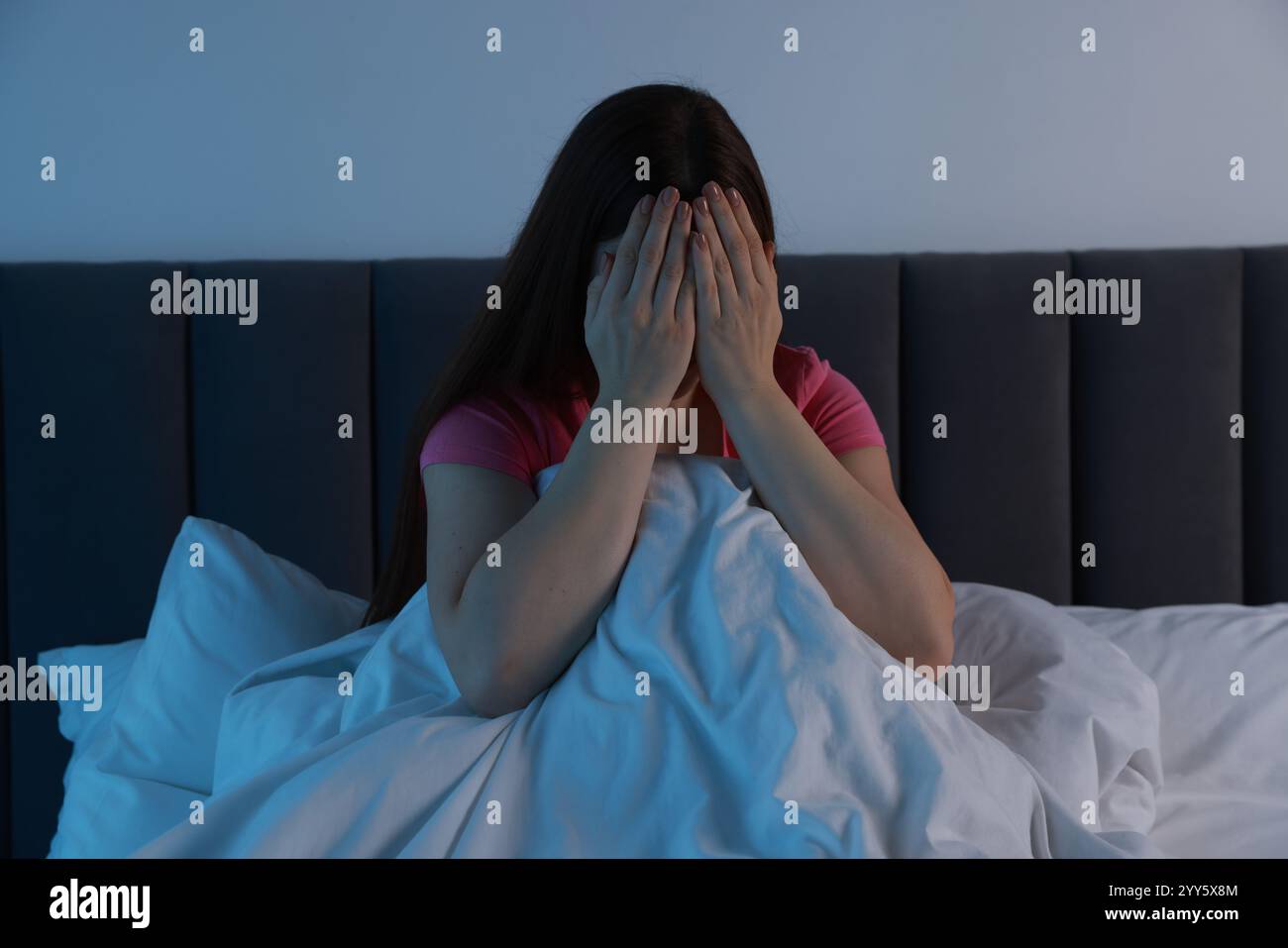 Fear of darkness. Scared young woman on bed and hiding her face in room ...