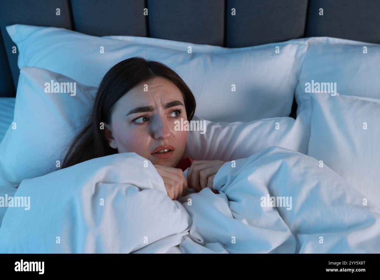 Fear of darkness. Scared young woman lying on bed in room at night ...