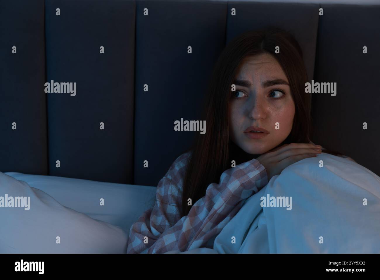 Fear of darkness. Scared young woman lying on bed in room at night ...