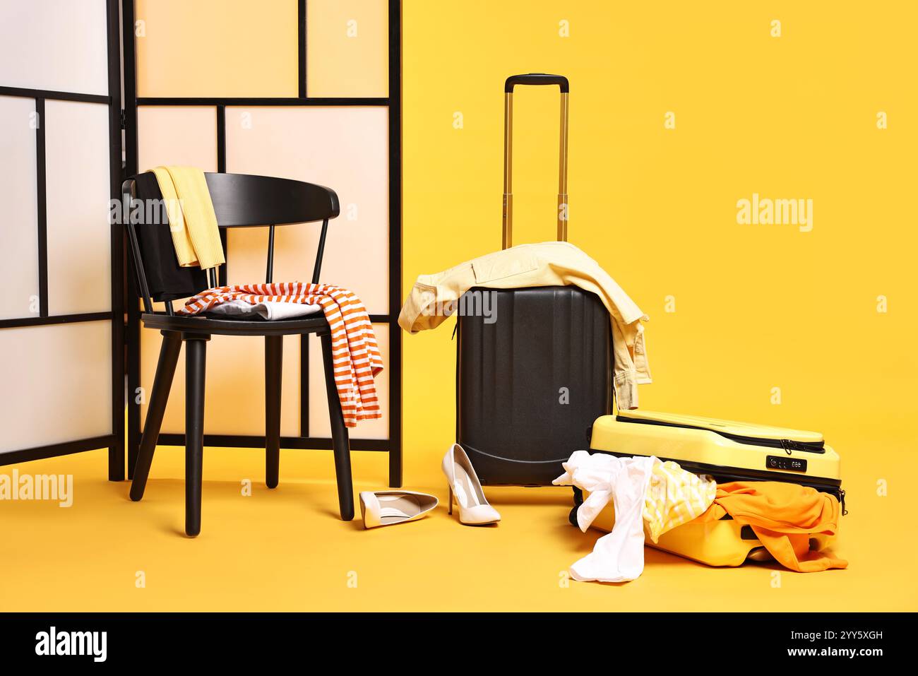 Suitcase with messy pile of clothes and chair on yellow background ...
