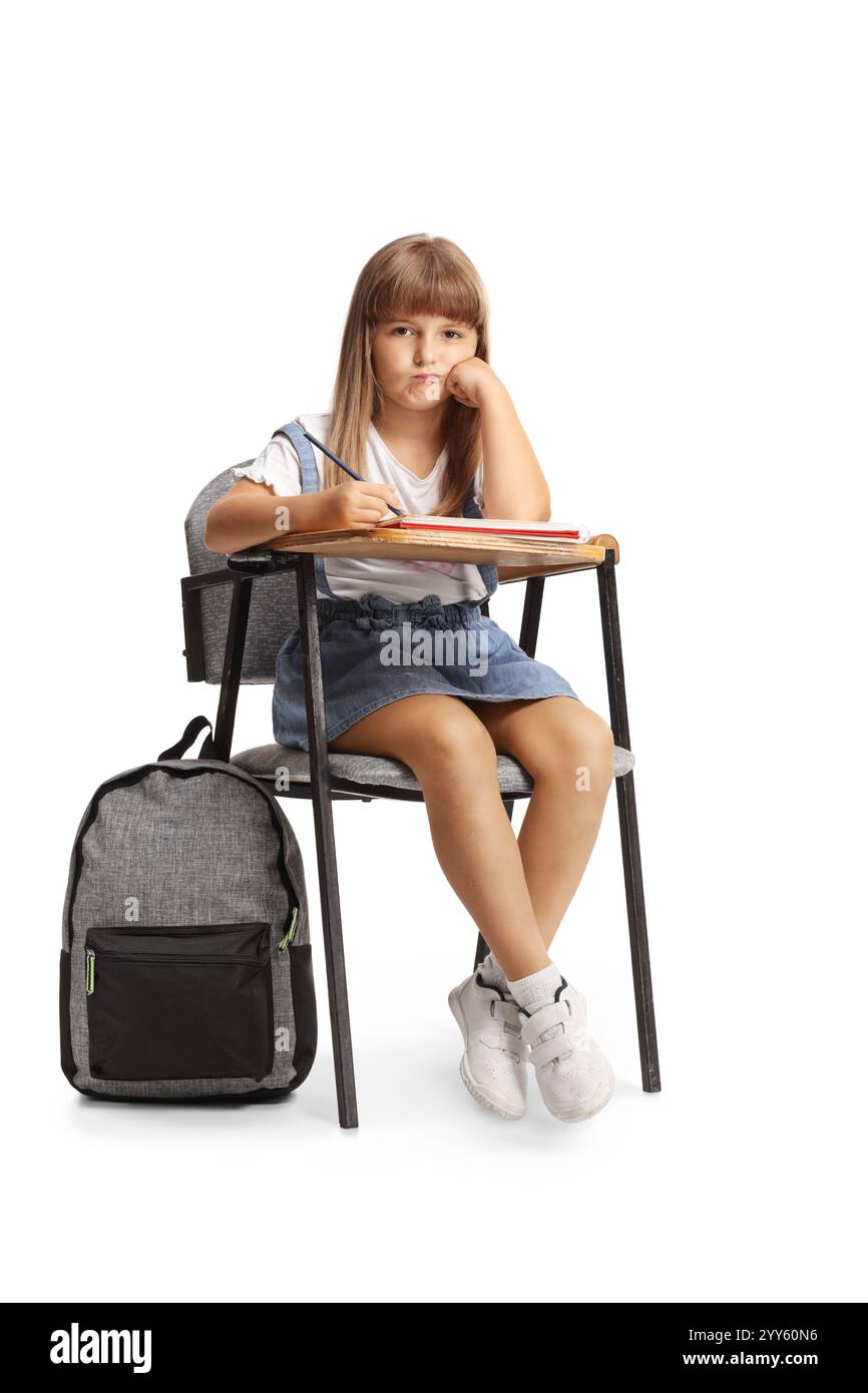 Grumpy little girl sitting in a school chair isolated on white ...