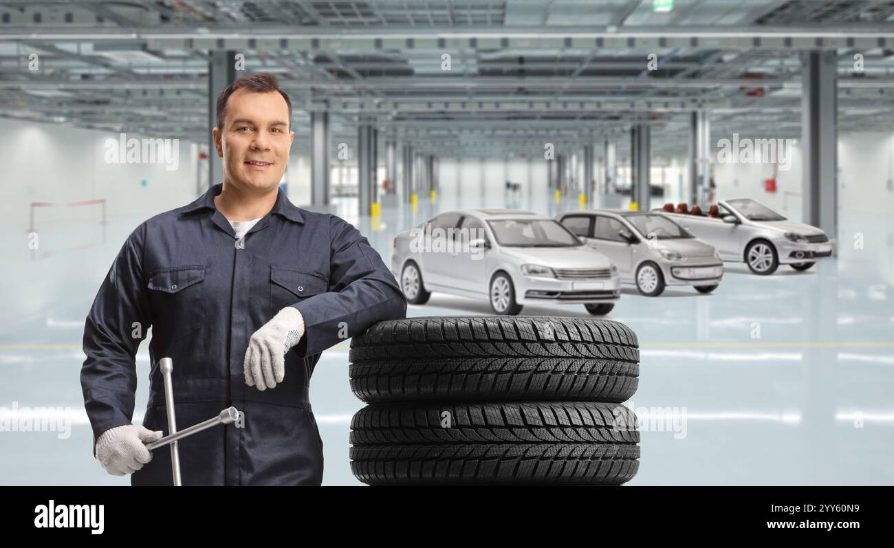 Auto mechanic worker in a uniform leaning on a pile of tires and ...