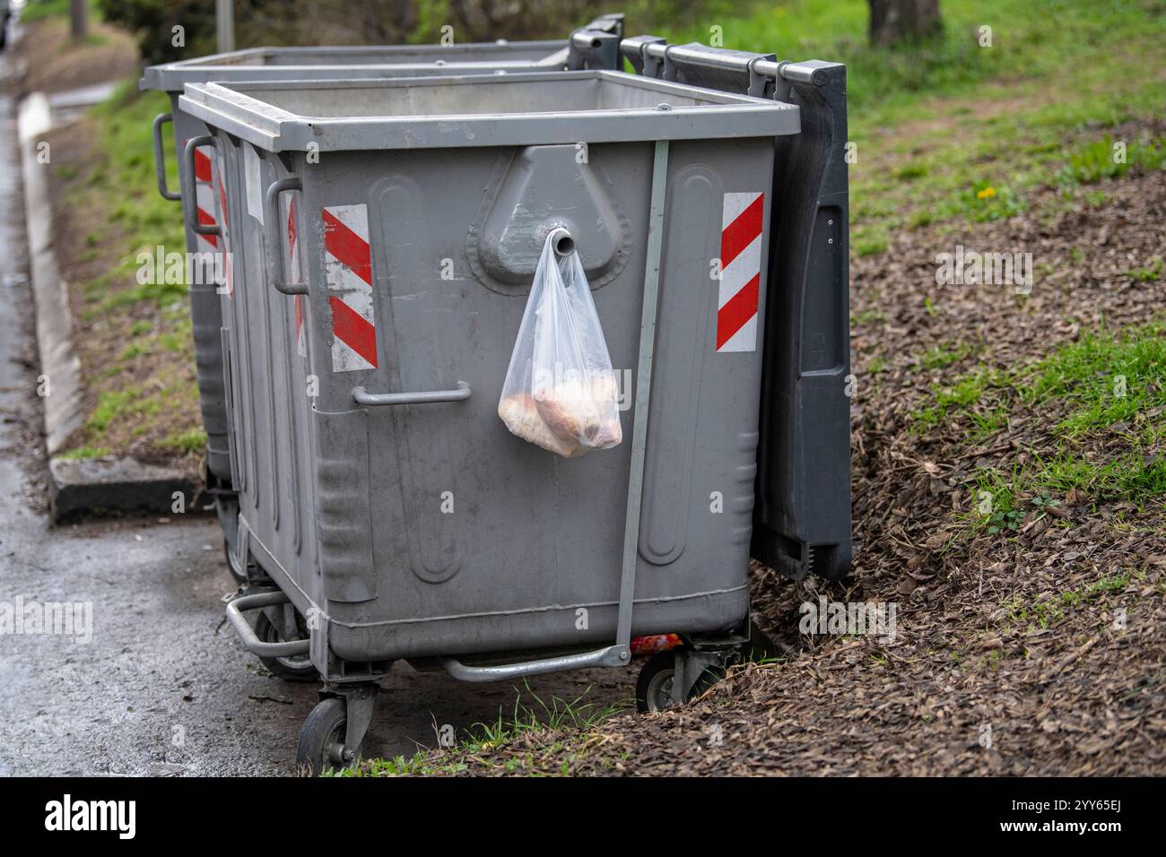 A plastic white bag with bread in it, hang on metal garbage dumpster ...