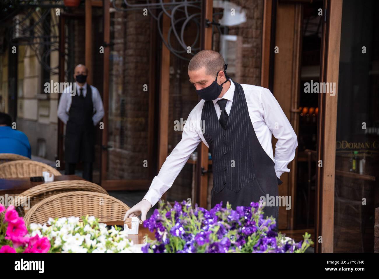 Young waiter wearing protective face mask while cleaning tables in ...