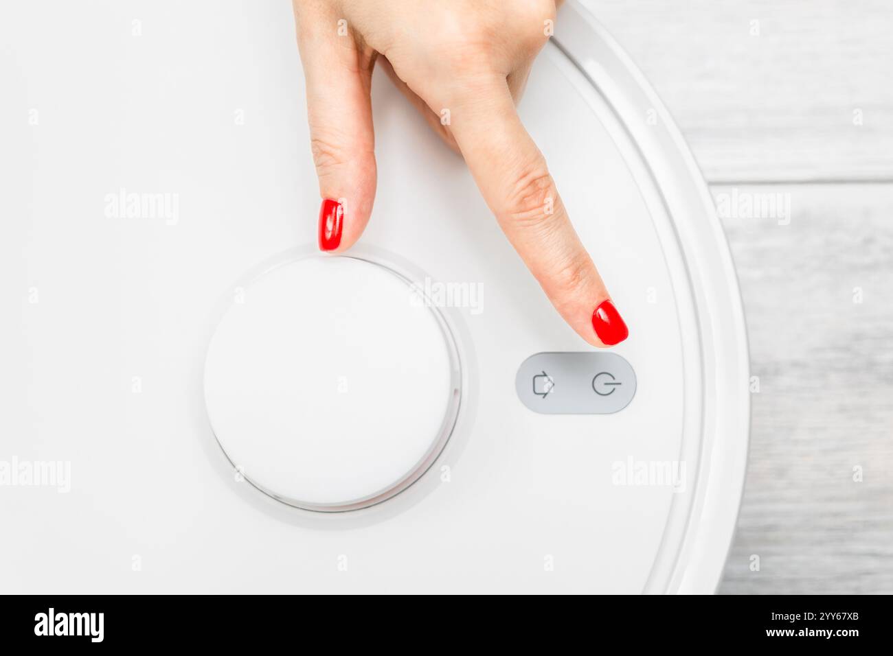 a woman's finger presses the power button of a robot vacuum cleaner ...