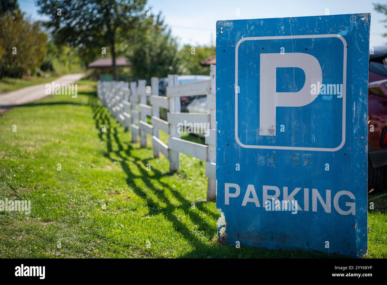 Big blue parking sign, leaning against old wooden white cattle fence, on a countryside road. A ...
