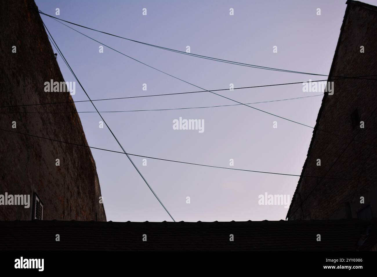 Electrical wires run between two old brick buildings. Sky in background ...