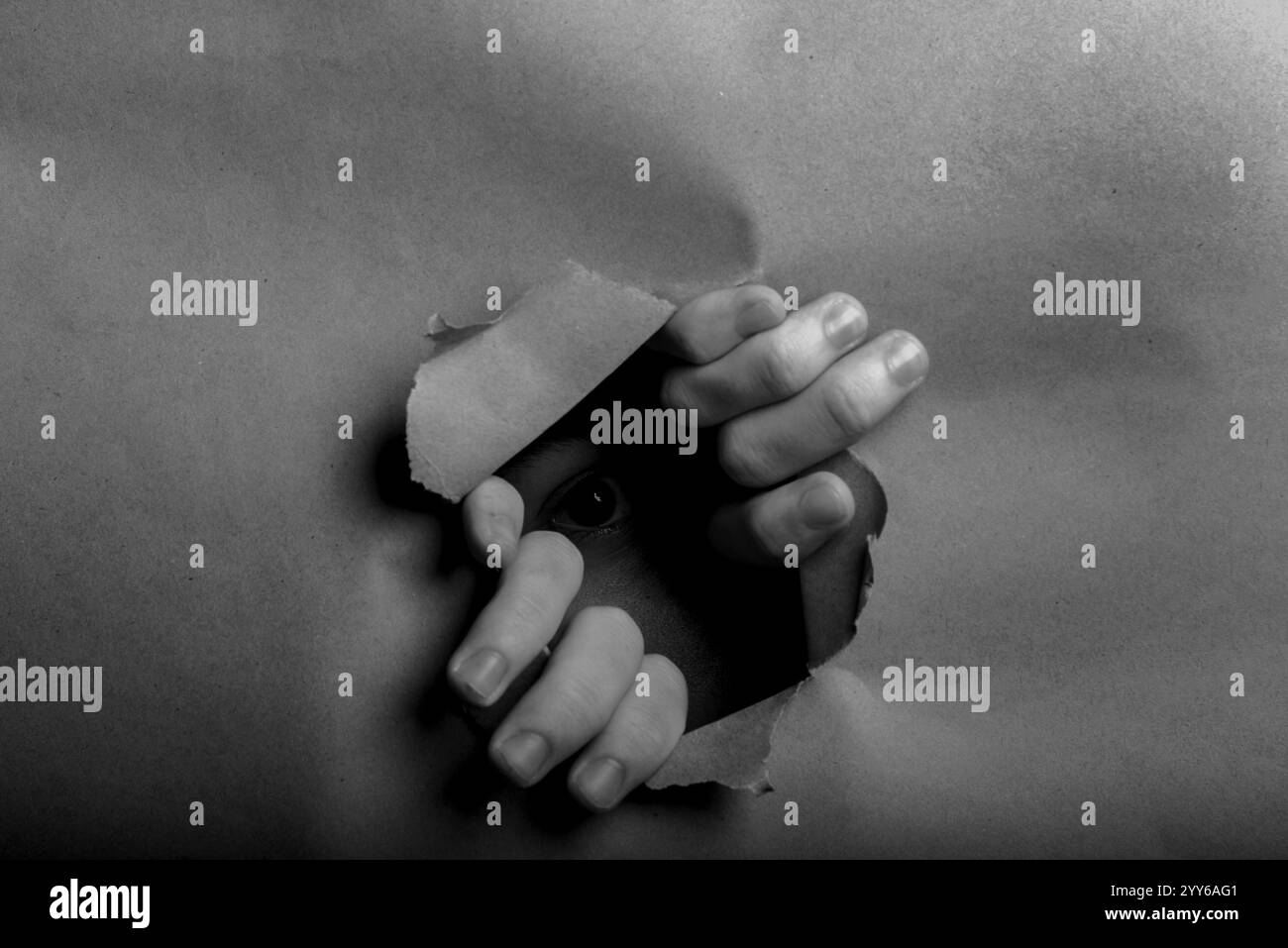 Man looking through a paper hole with his hands pushing the paper aside ...