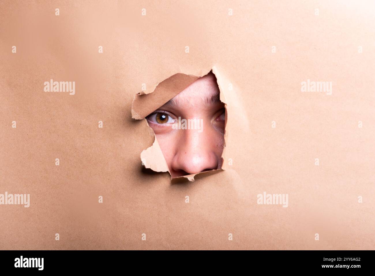 Man eye looking through a hole in a sheet of paper. Studio portrait ...