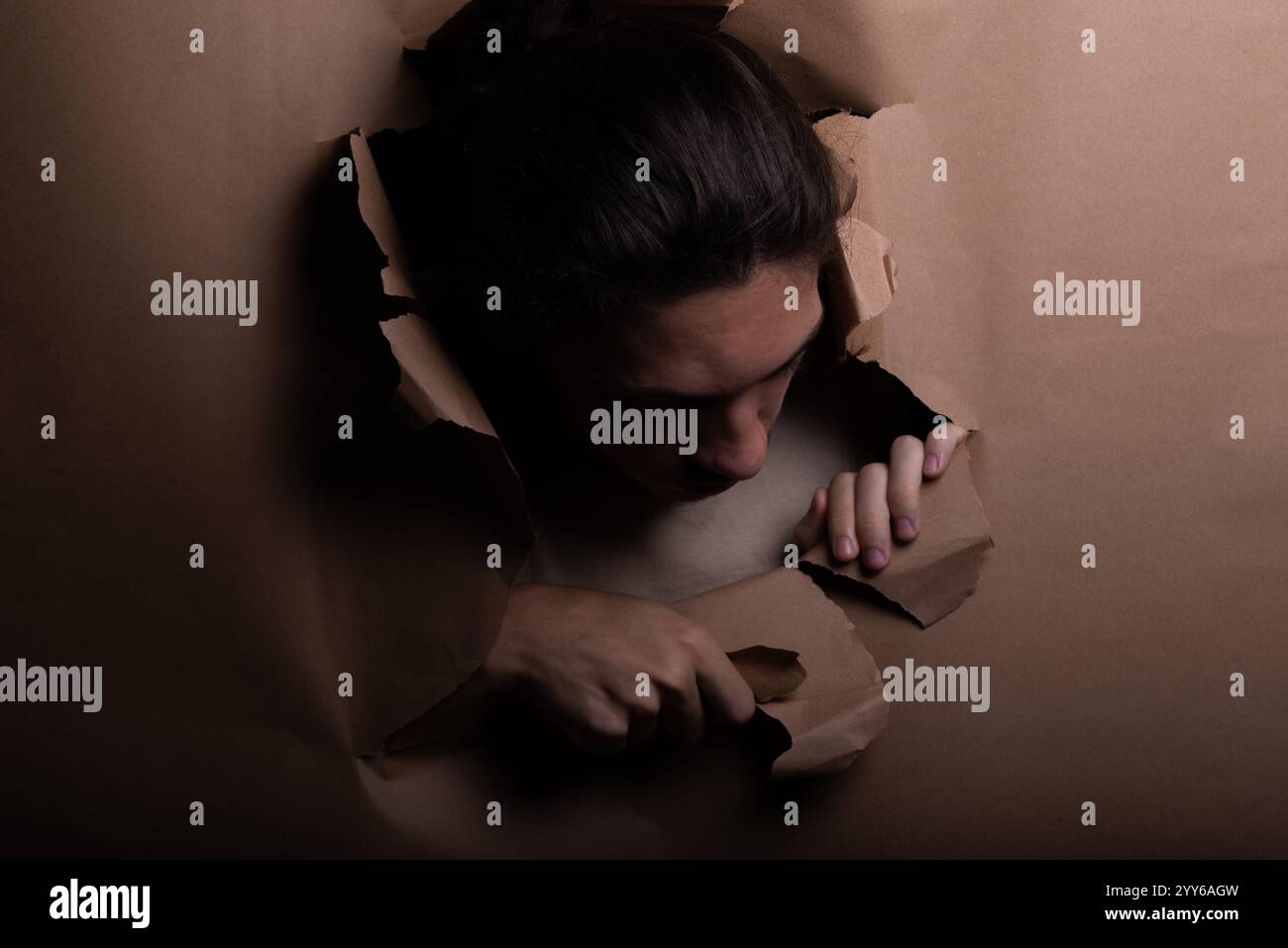 Man's head sticking out and looking through a paper hole with his hands ...