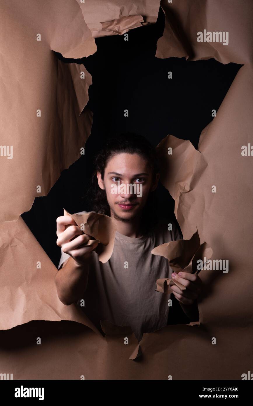 A man coming out through a hole in a sheet of brown paper. Tearing with ...