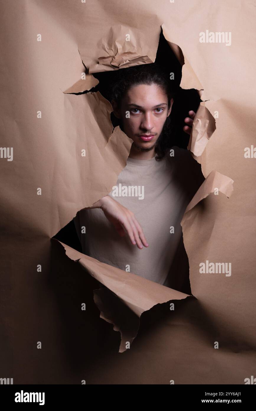 A man peering through a hole in a sheet of brown paper. Tearing the ...