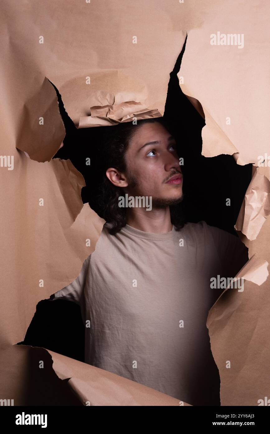 A man peering through a hole in a sheet of brown paper. Tearing the ...