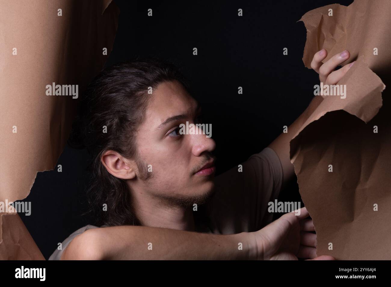 A man peering through a hole in a sheet of brown paper. Tearing the ...