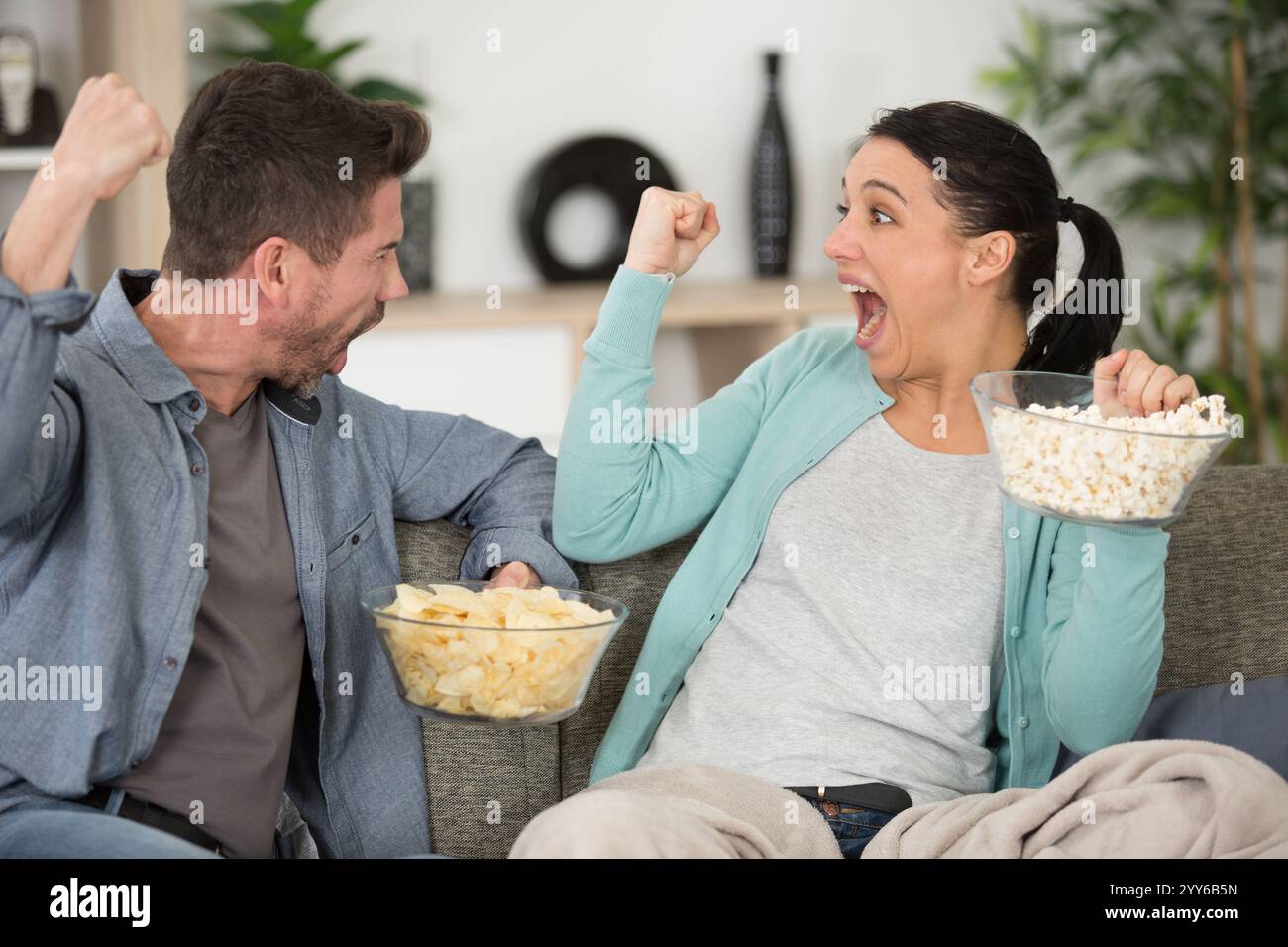 couple eating popcorn together and watching tv on sofa Stock Photo - Alamy