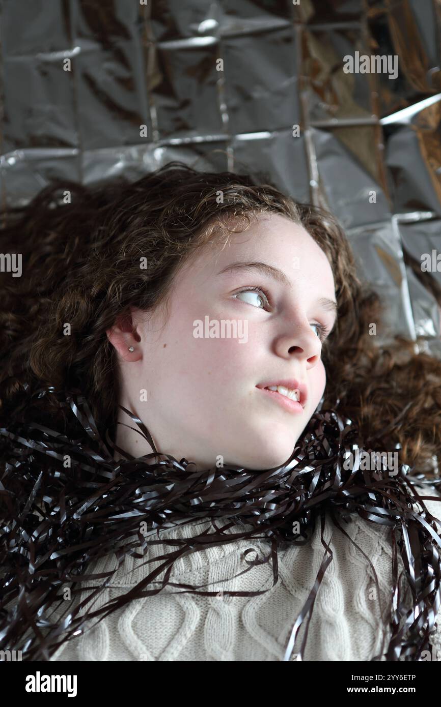 Teenage girl lying on silver background with cassette tape tangled ...