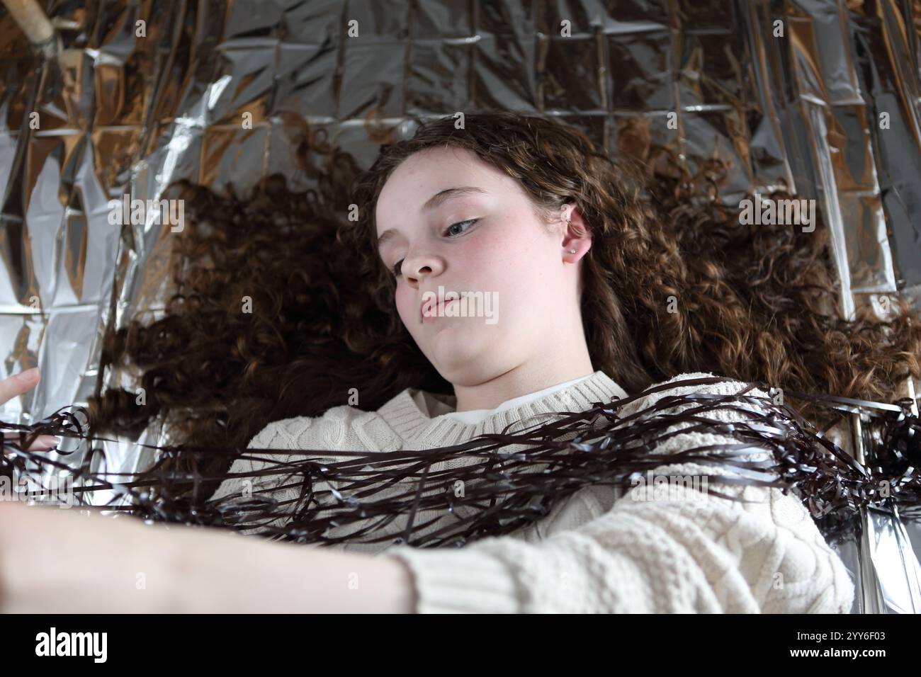 Teenage girl lying on silver background with cassette tape tangled ...