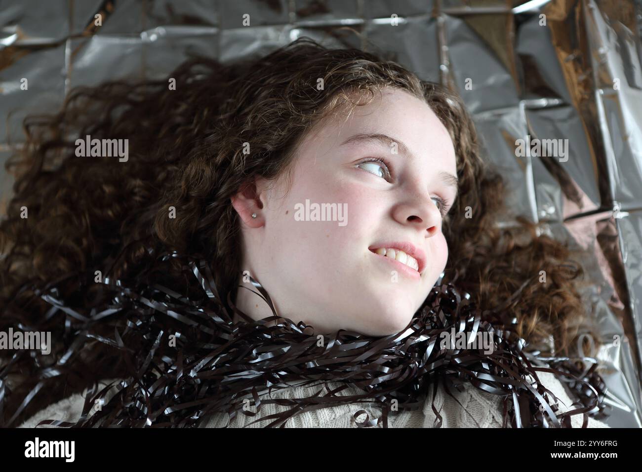 Teenage girl lying on silver background with cassette tape tangled ...