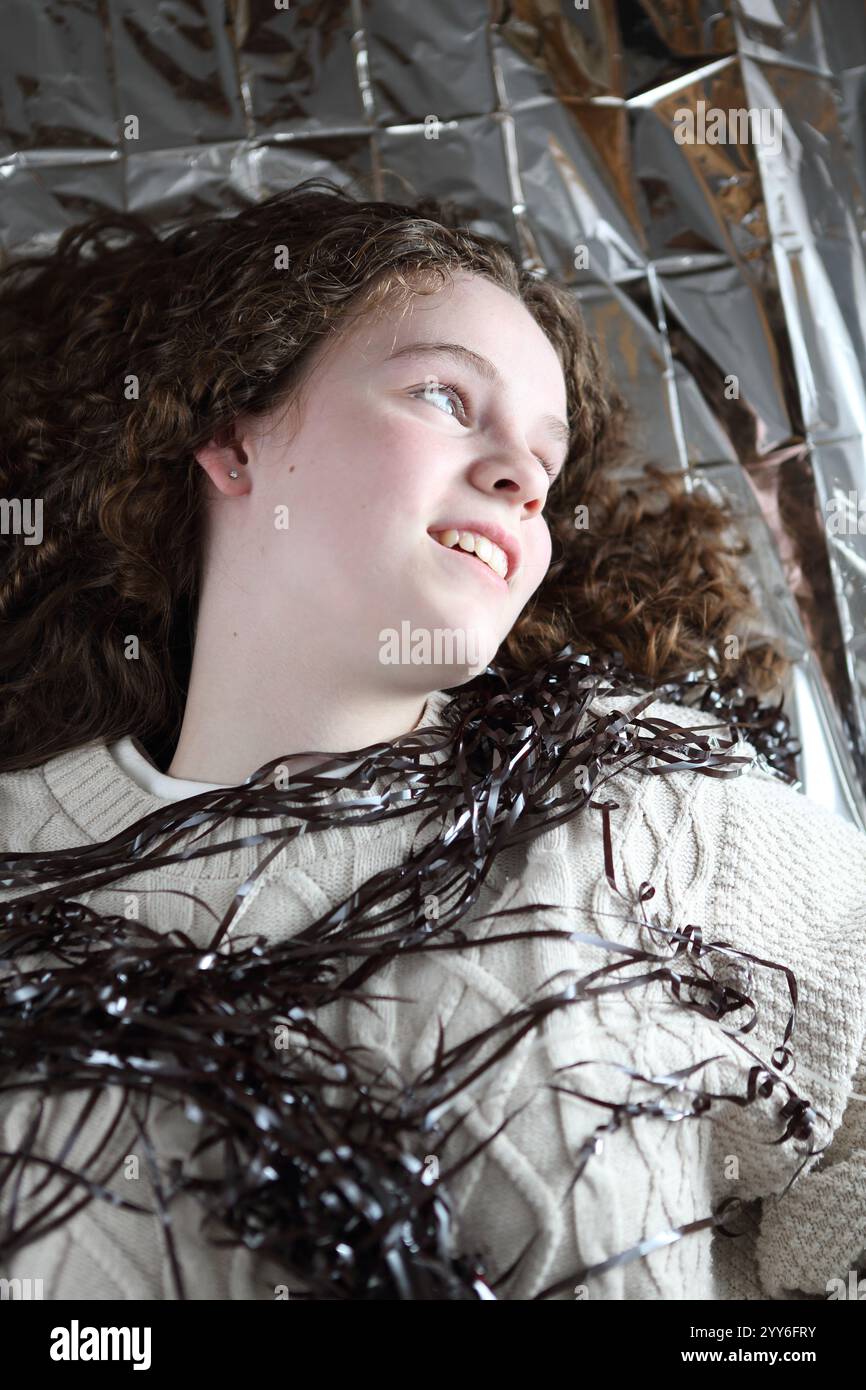 Teenage girl lying on silver background with cassette tape tangled ...