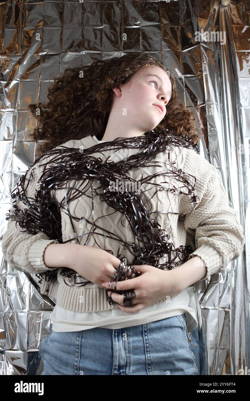 Teenage girl lying on silver background with cassette tape tangled ...