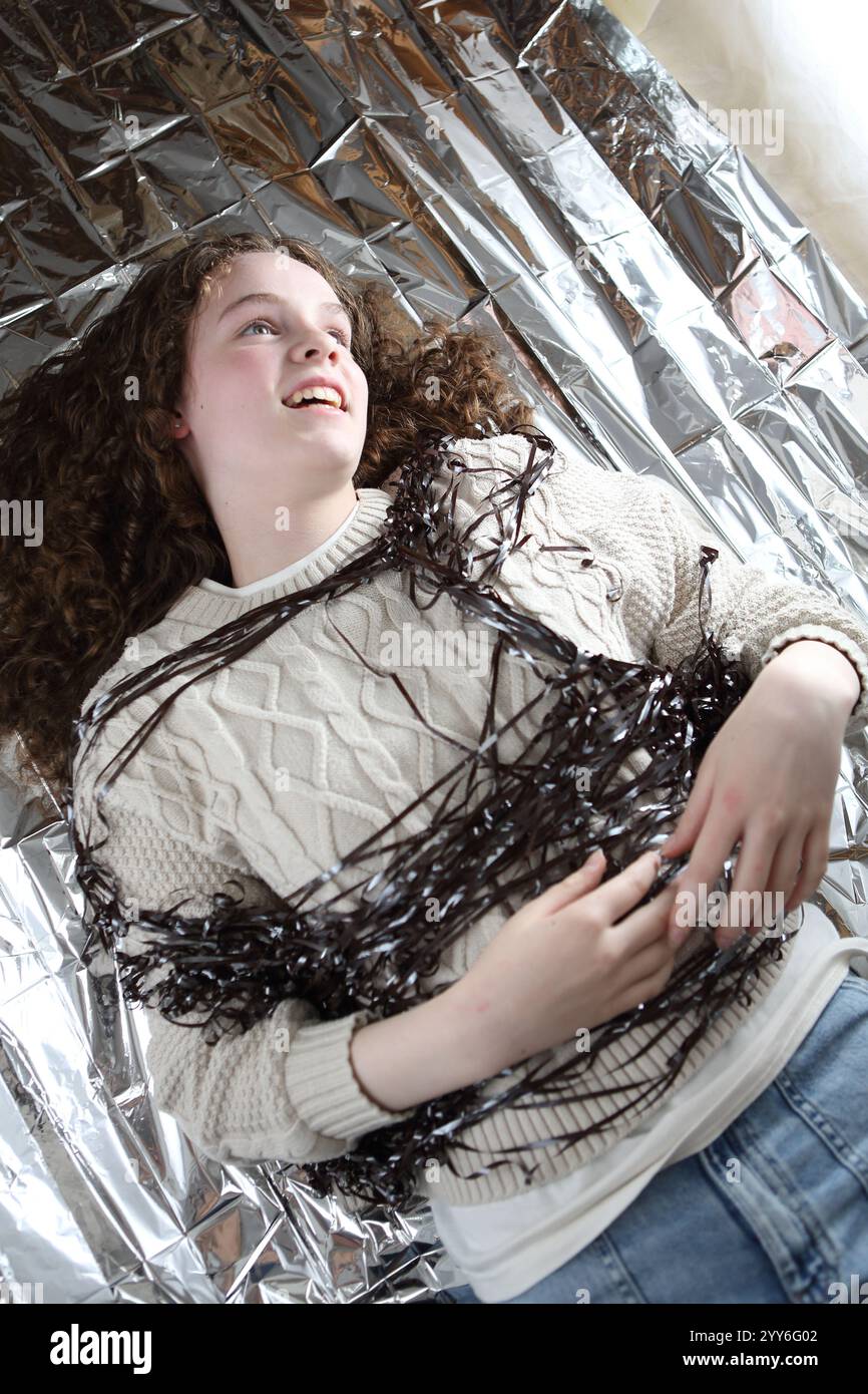 Teenage girl lying on silver background with cassette tape tangled ...