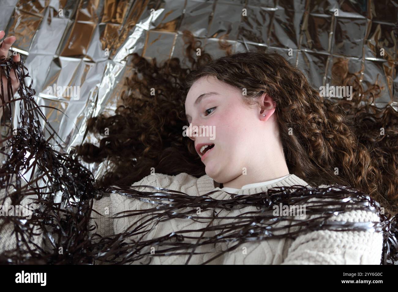 Teenage girl lying on silver background with cassette tape tangled ...