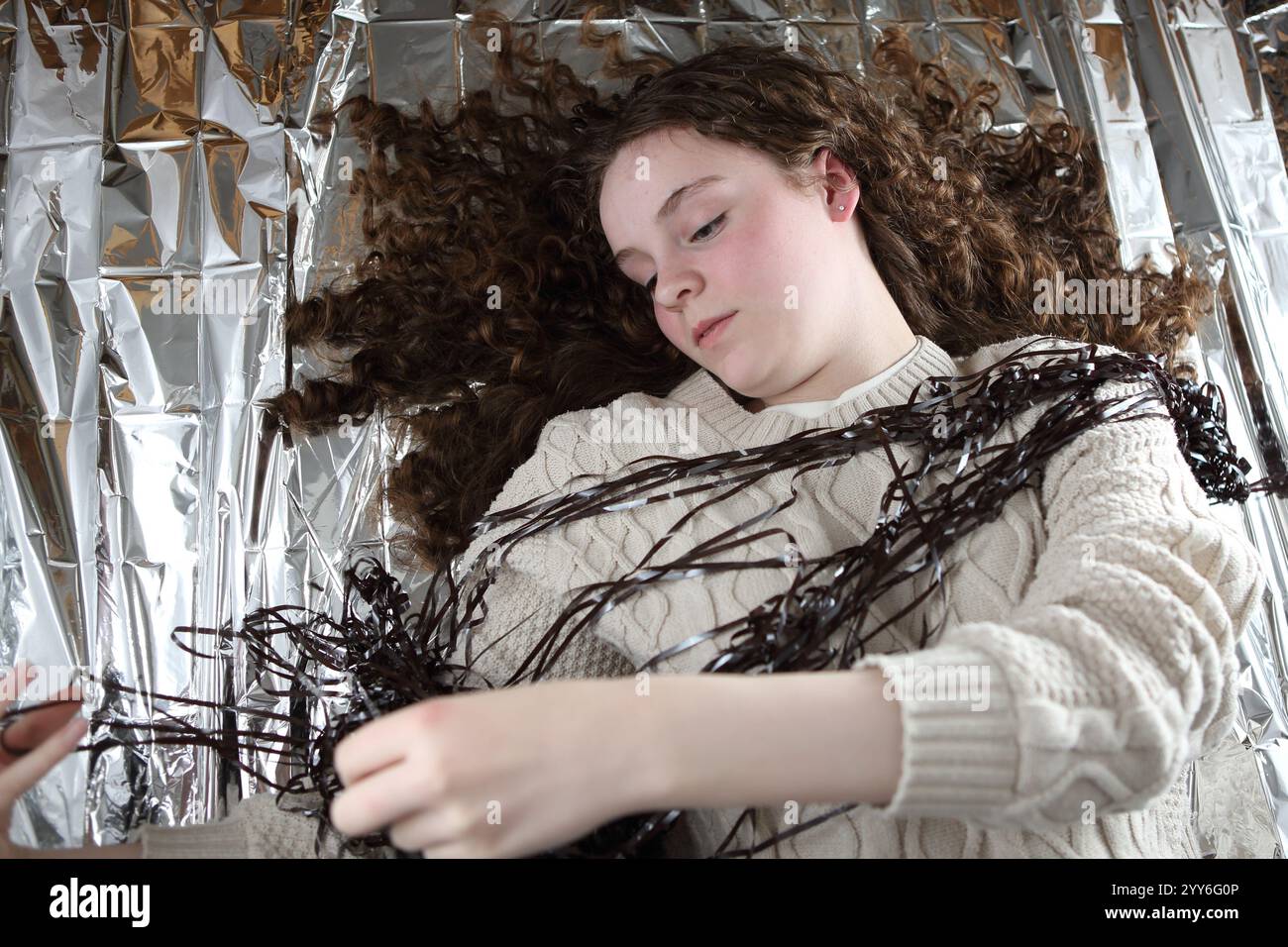 Teenage girl lying on silver background with cassette tape tangled ...