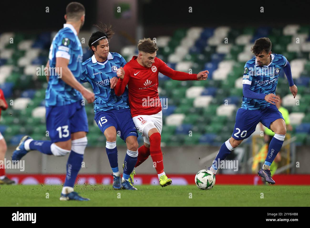 Larne's Sean Graham (centre) battles for the ball with Gent's Atsuki ...