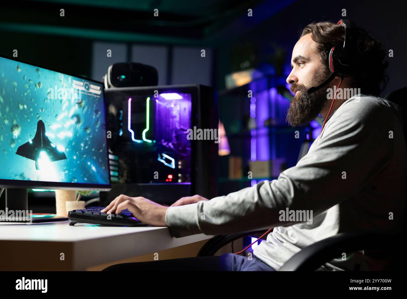 Man using gaming keyboard and headphones to play spaceship flying game ...
