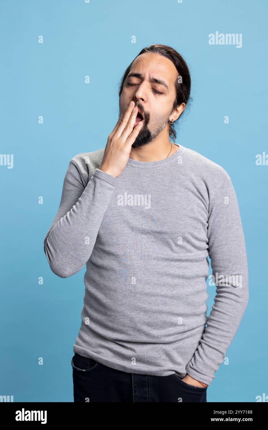 Young adult yawning and feeling very tired against blue background ...