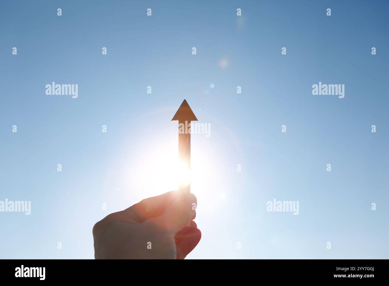 Hands holding up a rising arrow towards the sunrise sun, stock finance ...