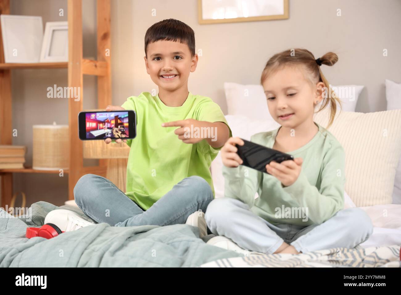 Cute happy little kids with mobile phones playing video games on bed at ...