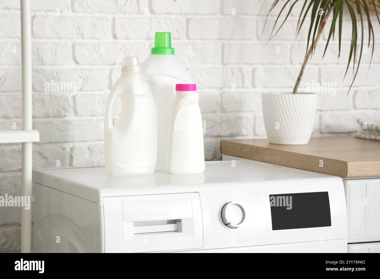 Washing machine with bottles of laundry detergent near white brick wall ...