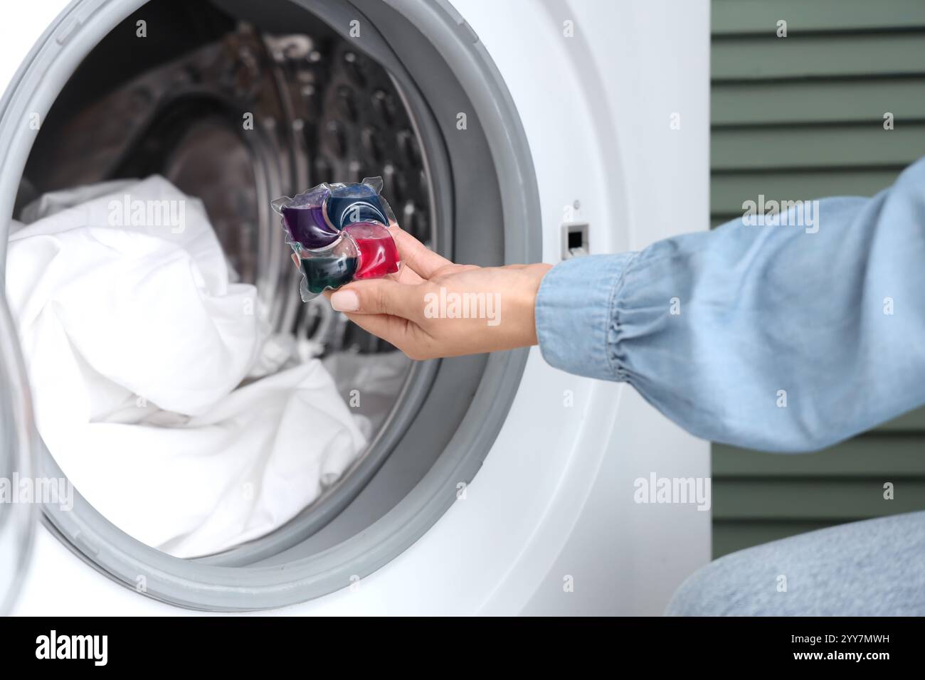 Woman putting gel capsule of laundry detergent into washing machine ...