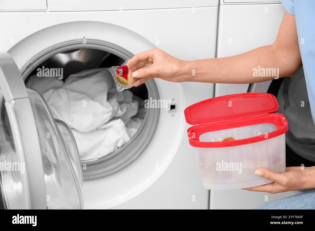 Woman putting gel capsule of laundry detergent into washing machine ...