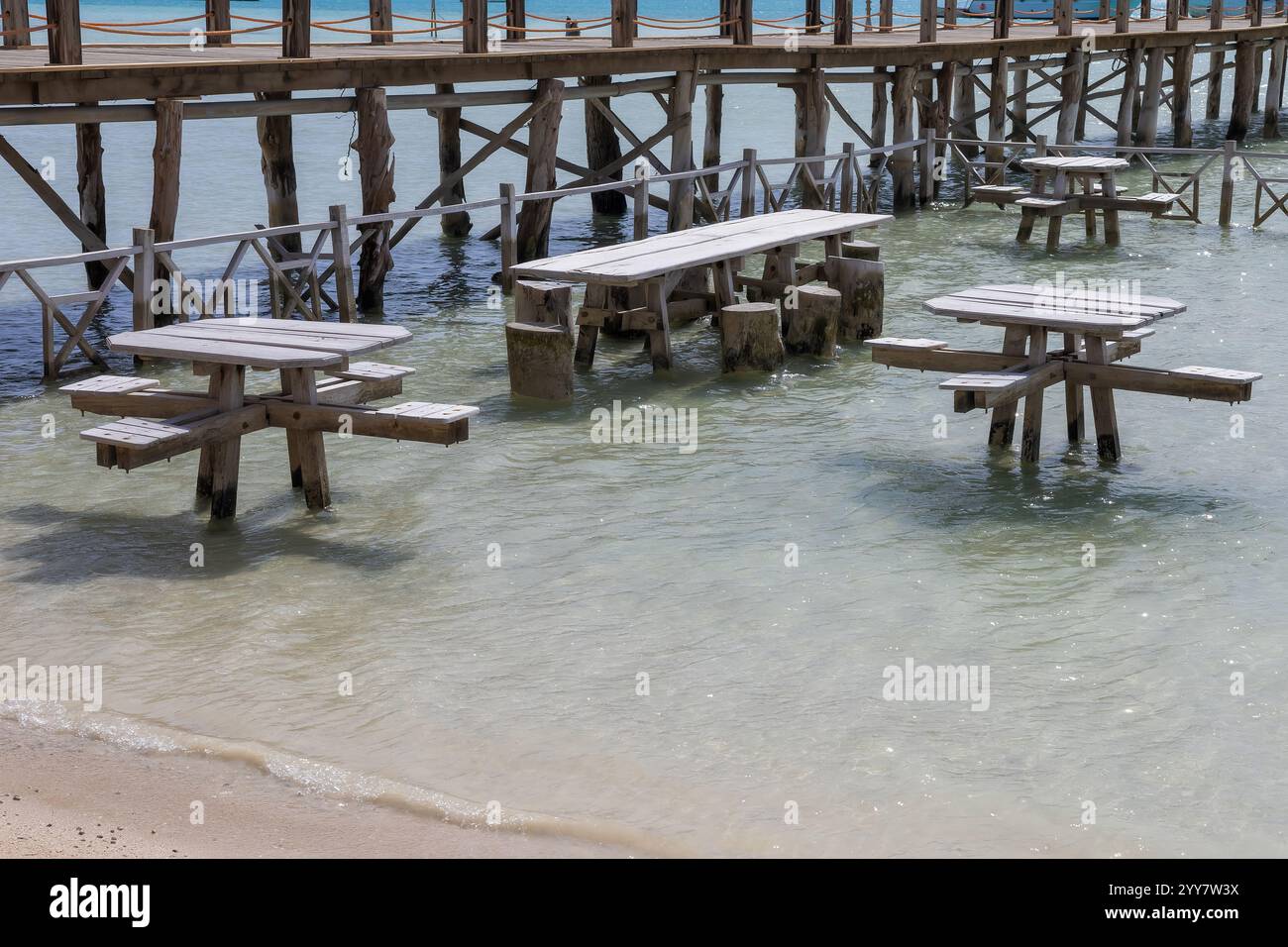 Serene image of a seaside pier featuring rustic wooden tables partially ...