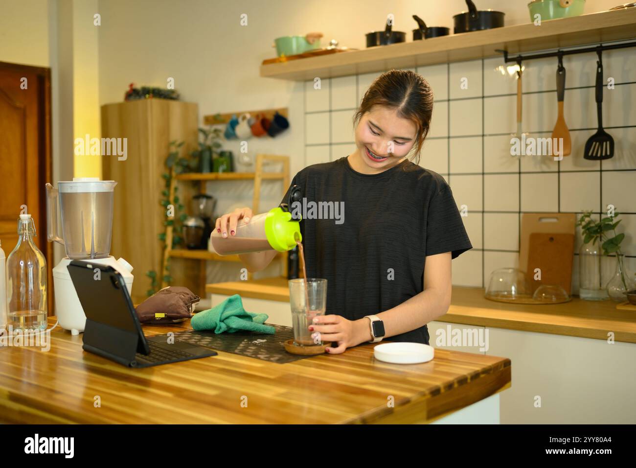Pretty young woman pouring chocolate protein shake into a glass from a ...