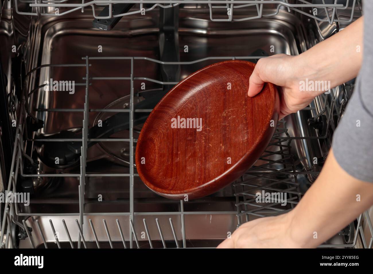 A woman's hand puts a wooden plate in the dishwasher - unsafe way, bad ...