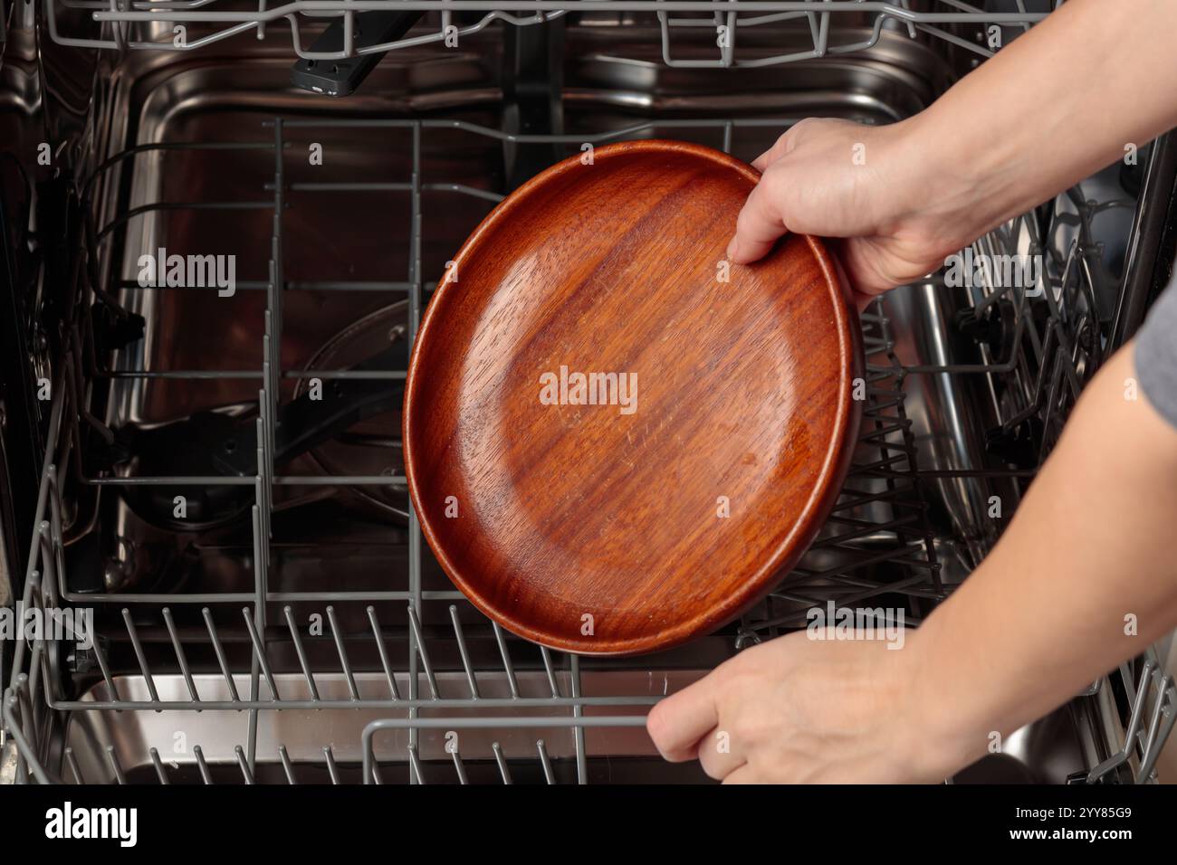 A woman's hand puts a wooden plate in the dishwasher - unsafe way, bad ...