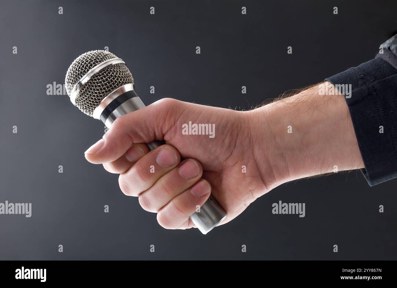 Hand holding metal handheld microphone with dark cloth jacket sleeve ...