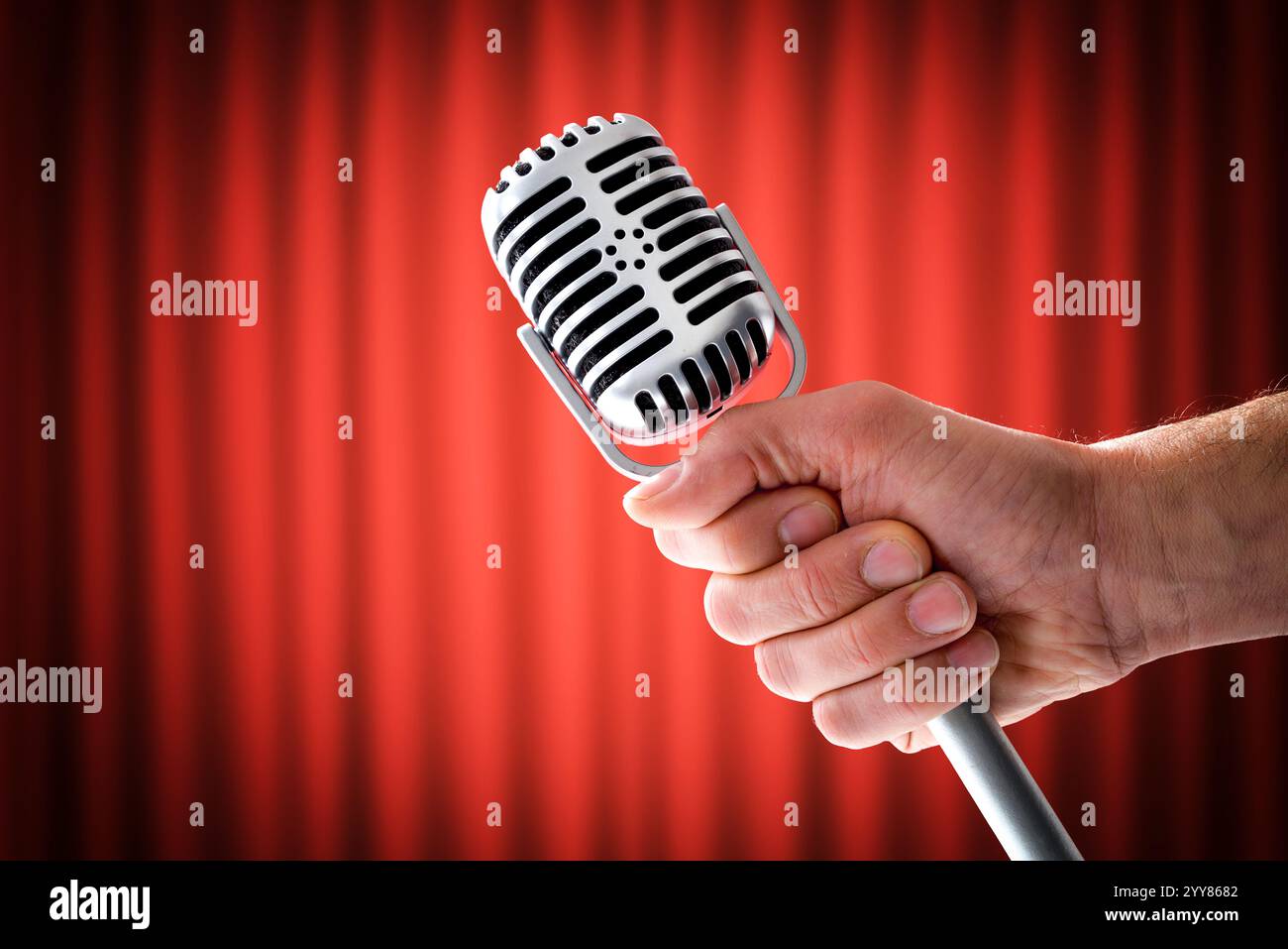 Hand holding a vintage microphone with mic stand on a stage with red ...