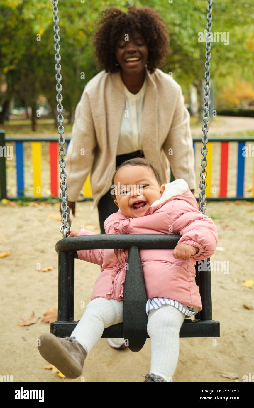 Happy baby girl swinging at playground with mother pushing Stock Photo - Alamy