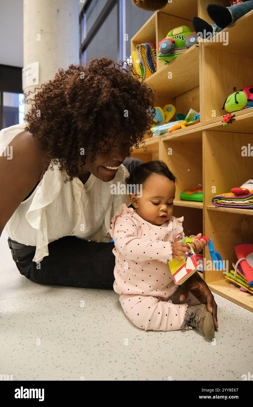 Babysitter smiling and playing with baby girl in nursery Stock Photo ...