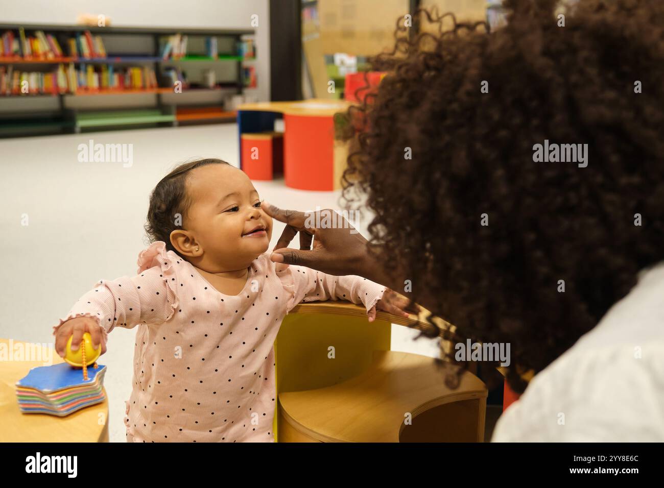 Librarian playing with baby girl in library reading room Stock Photo ...